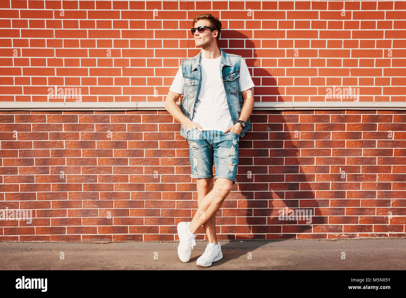 casual young man stands with his back against a brick wall Stock Photo ...