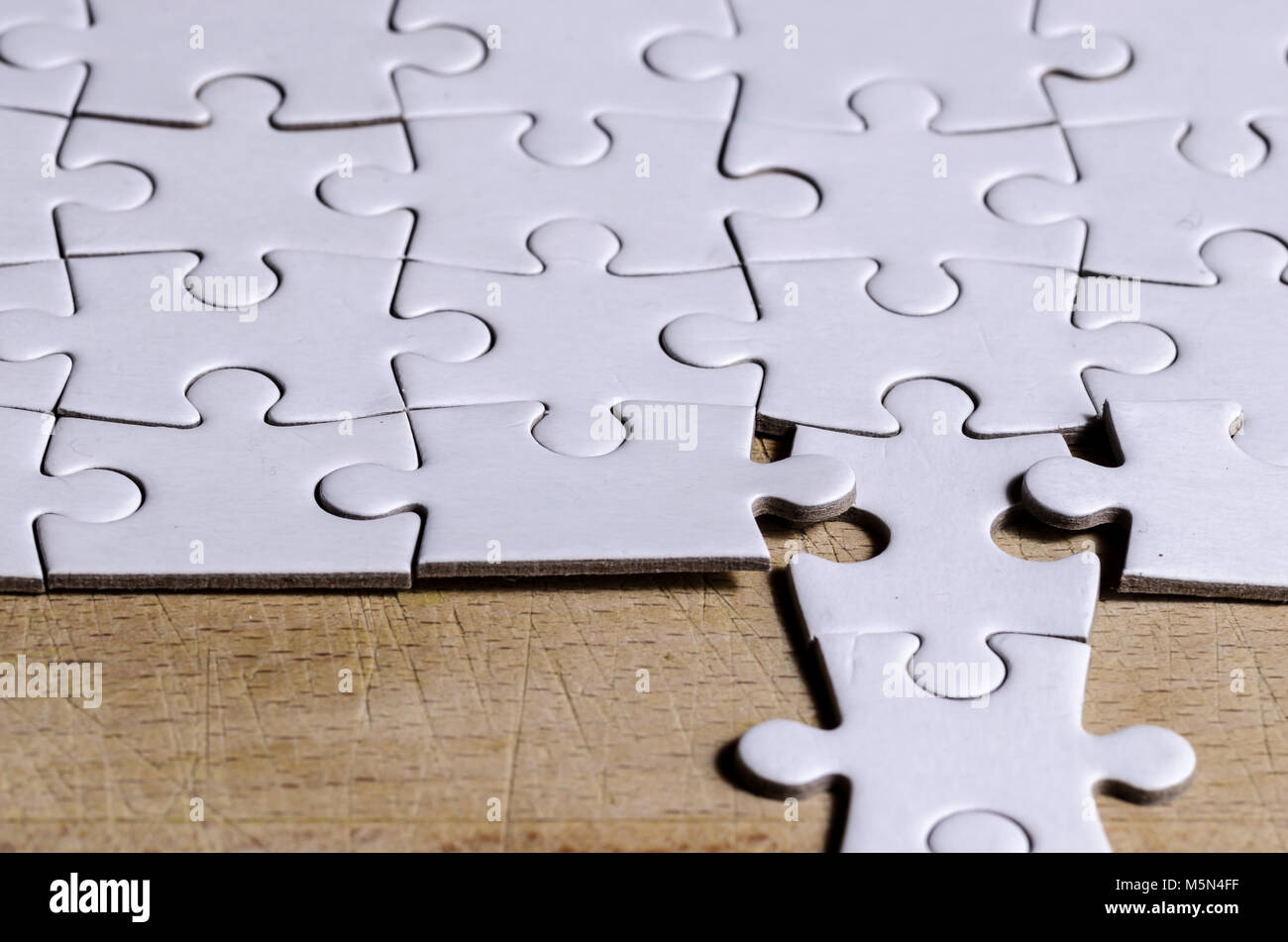 white jigsaw/puzzle with a row in wrong position, over wooden table ...
