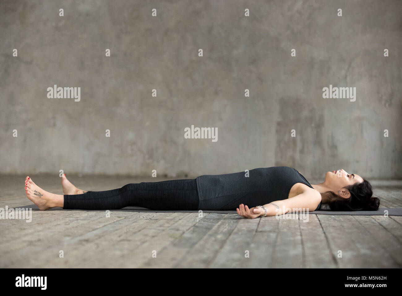 Young sporty woman practicing yoga, lying in Dead Body or Corpse pose ...