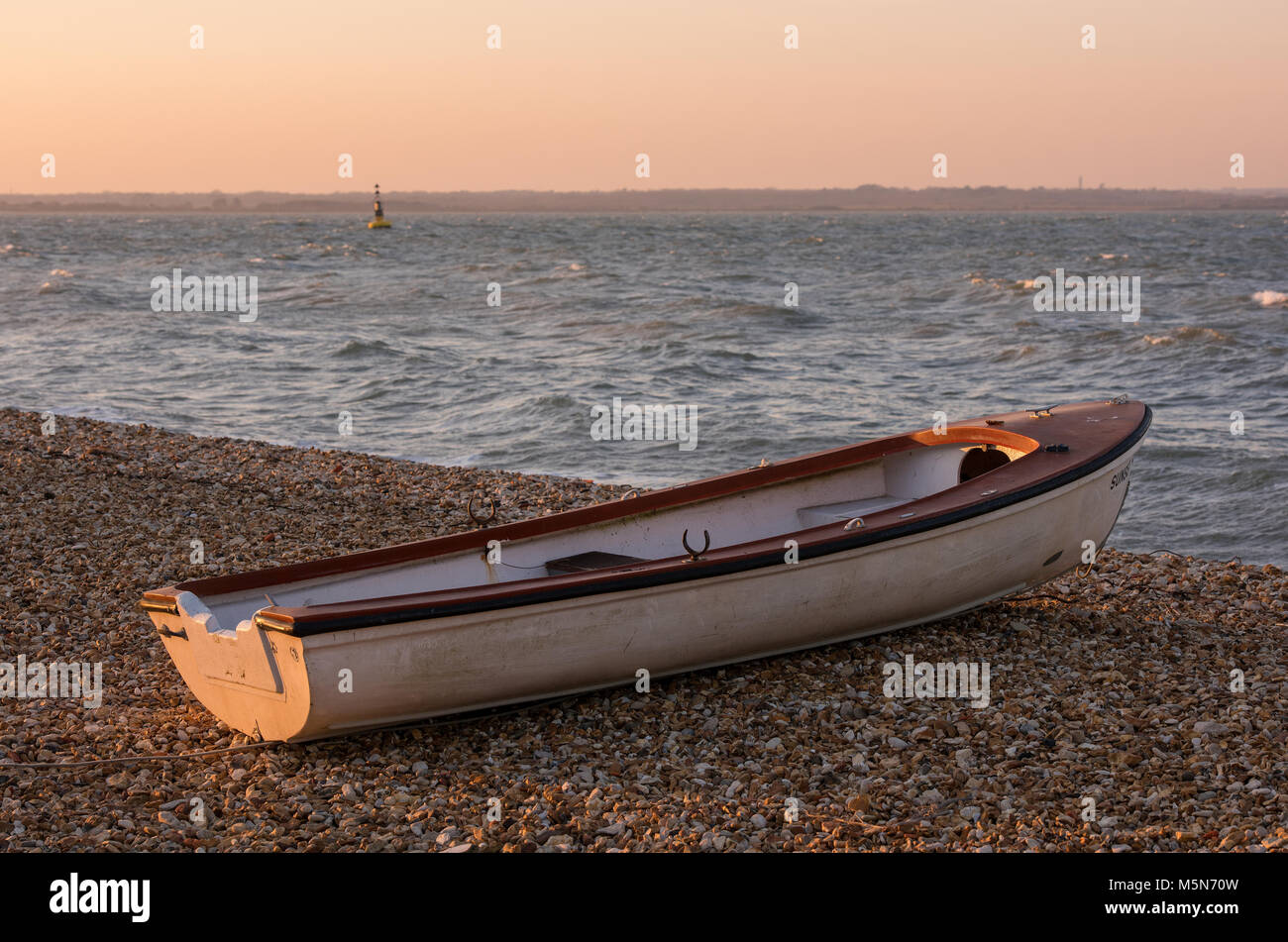An open boat rowing dinghy pulled up onto beach and resting on a ...