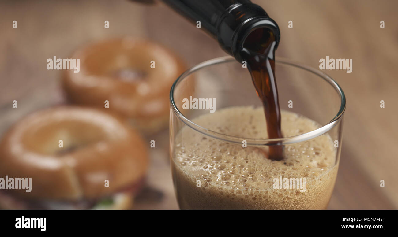 stout beer poring into glass with bagels on background, wide photo ...