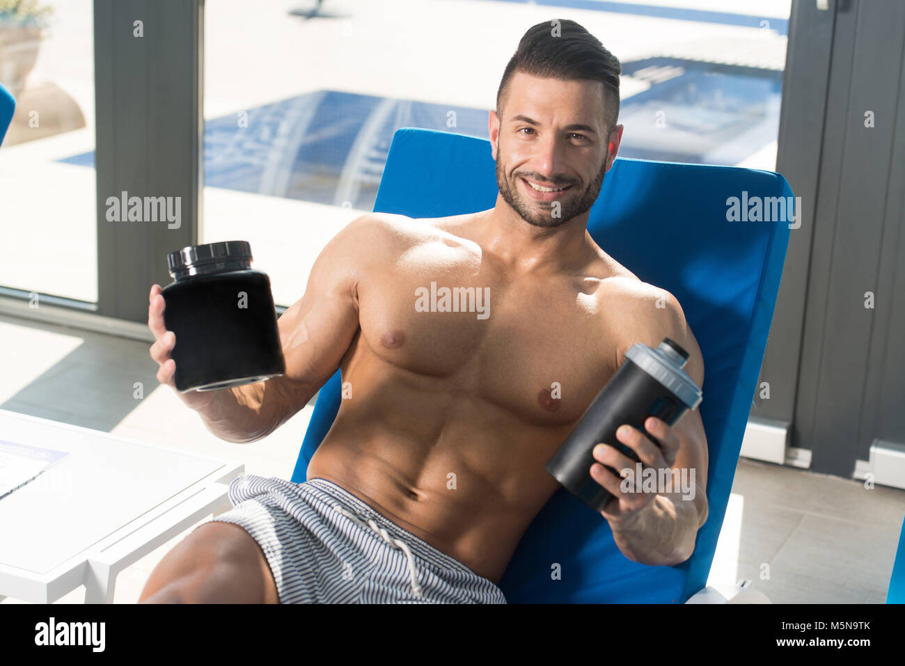 Young Man Resting On Sun Loungers By Swimming Pool With Supplements ...