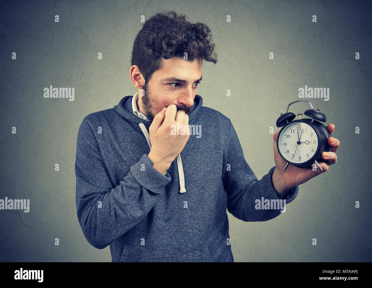 Young casual man holding clock and looking stressed with being late Stock Photo - Alamy