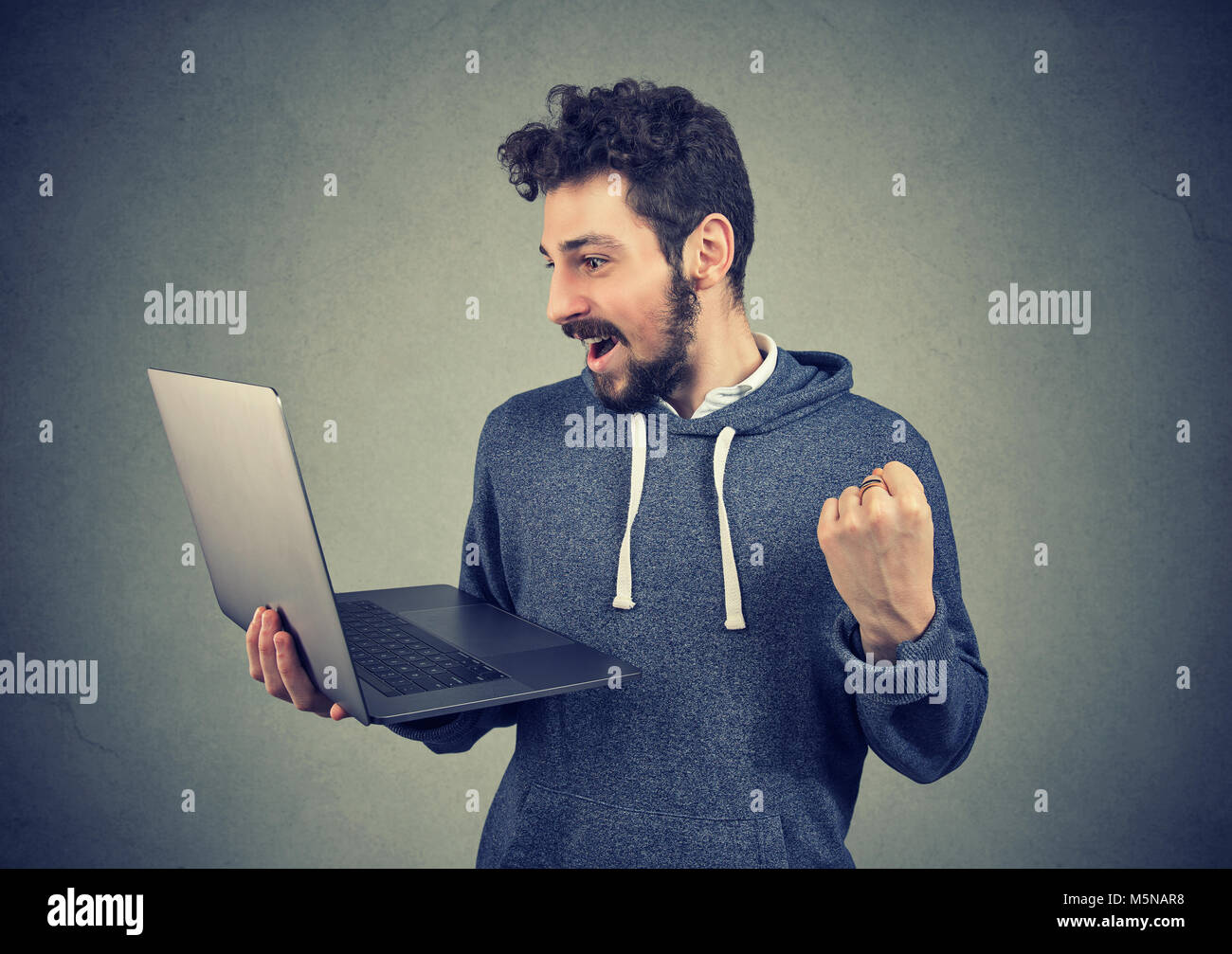Excited young man holding laptop and looking happy winning with fast ...