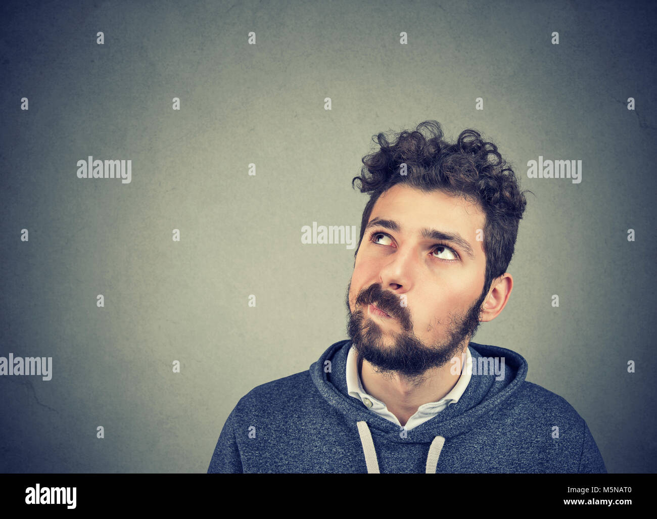 Young bearded man in puzzlement looking up and considering problem in ...