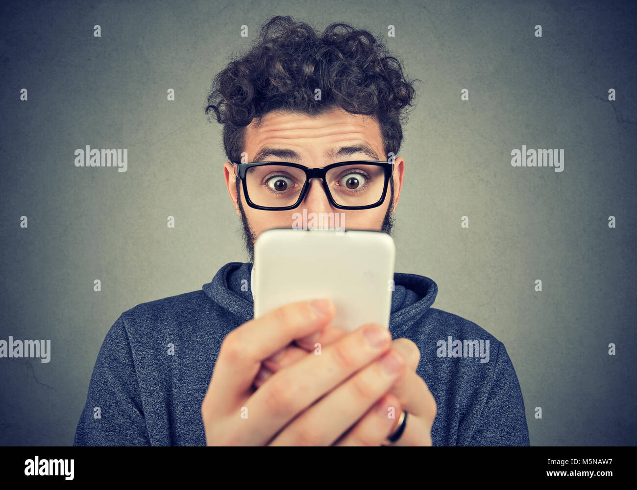 Young Bearded Man In Glasses Using Phone With Expression Of Great