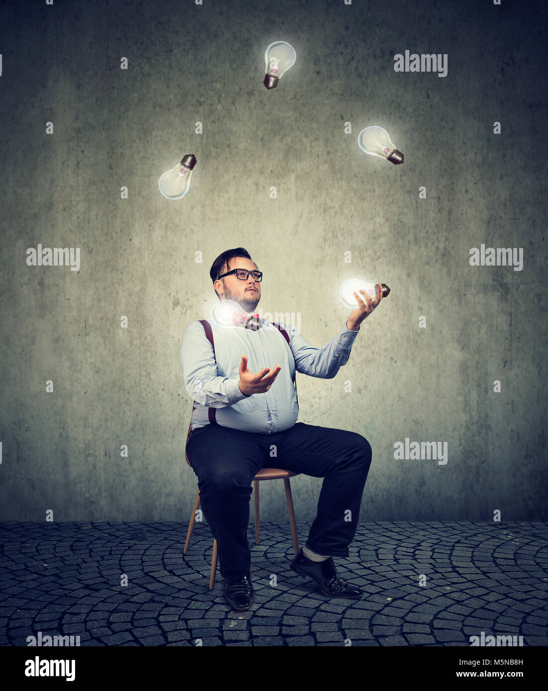 Young chubby man sitting on chair and juggling with light bulbs being ...
