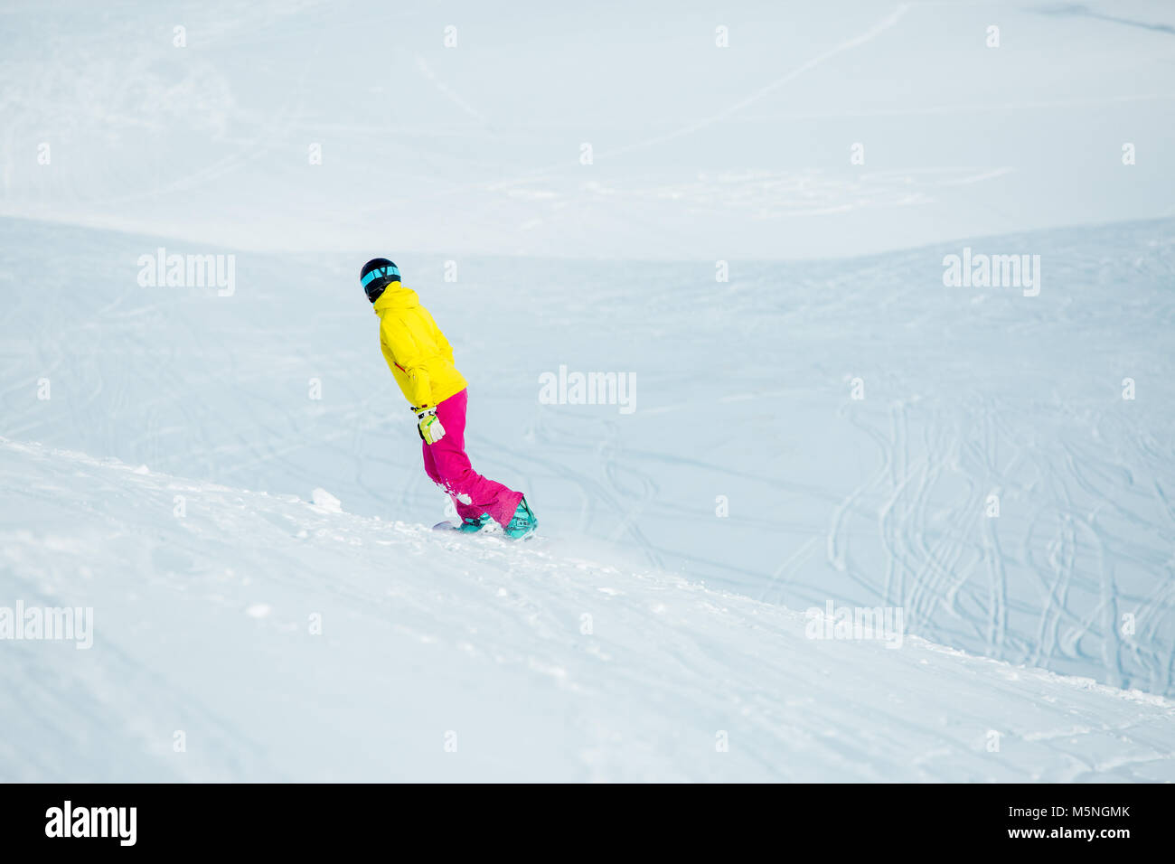 Picture from back of girl in sports clothes snowboarding in winter ...