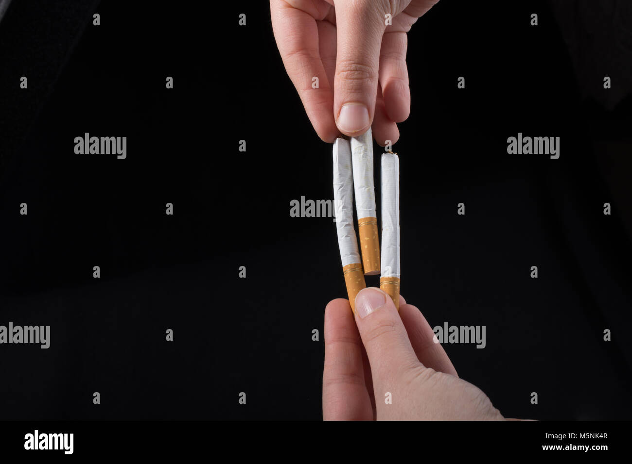 Hand is giving out cigarette on a black background Stock Photo - Alamy