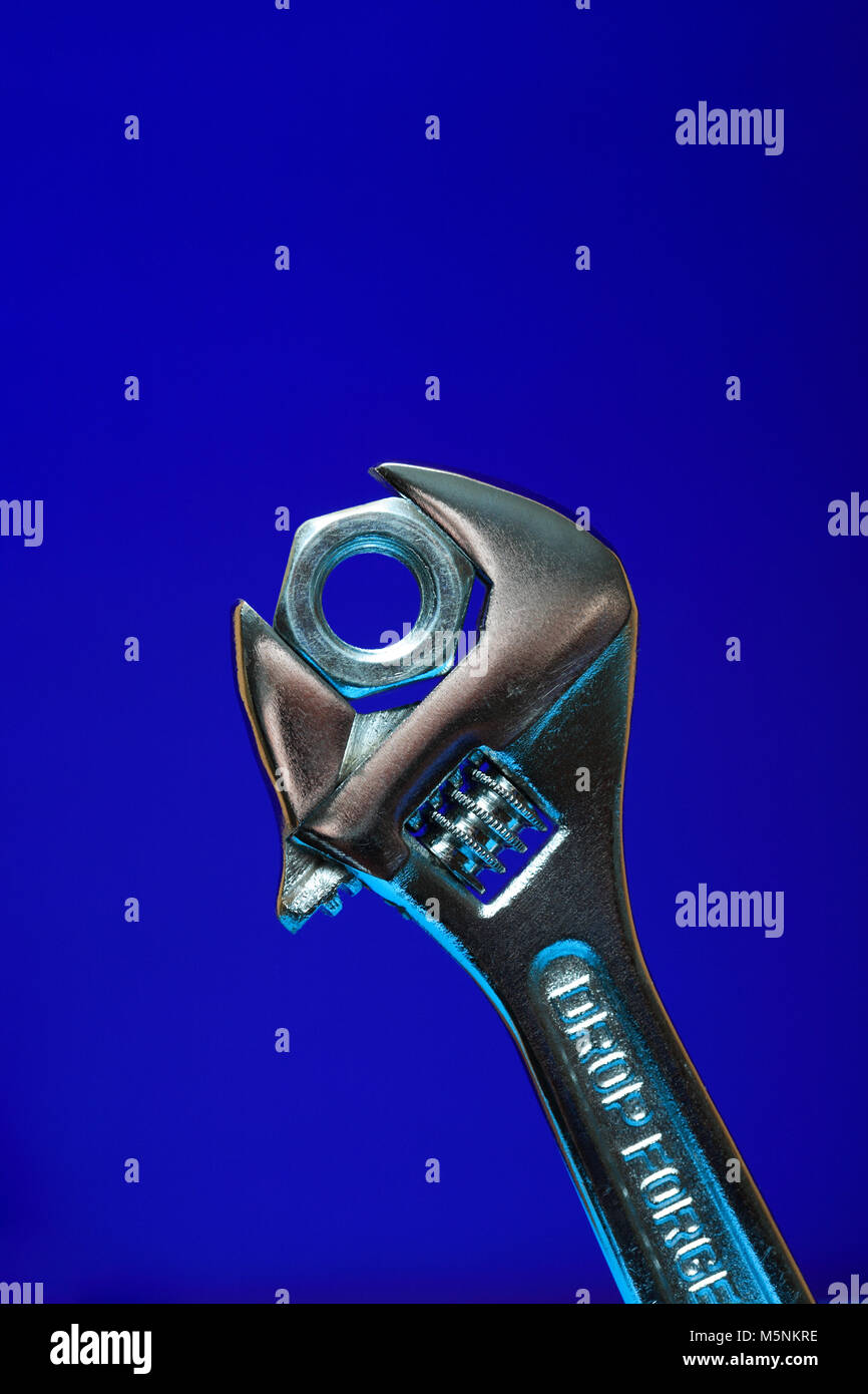 Extreme closeup of adjustable wrench gripping a screw nut on blue ...