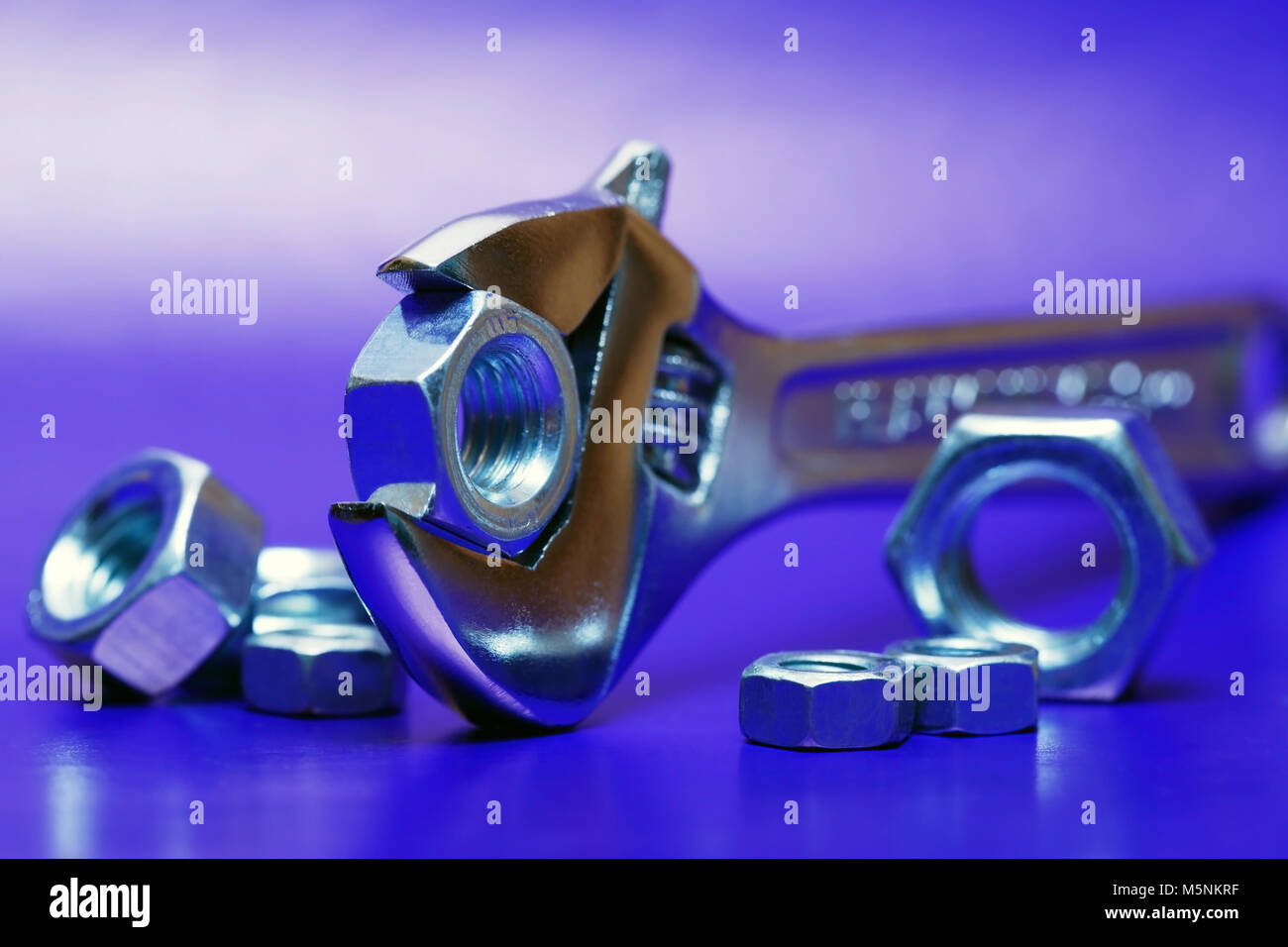 Extreme closeup of adjustable wrench gripping a screw nut on blue ...