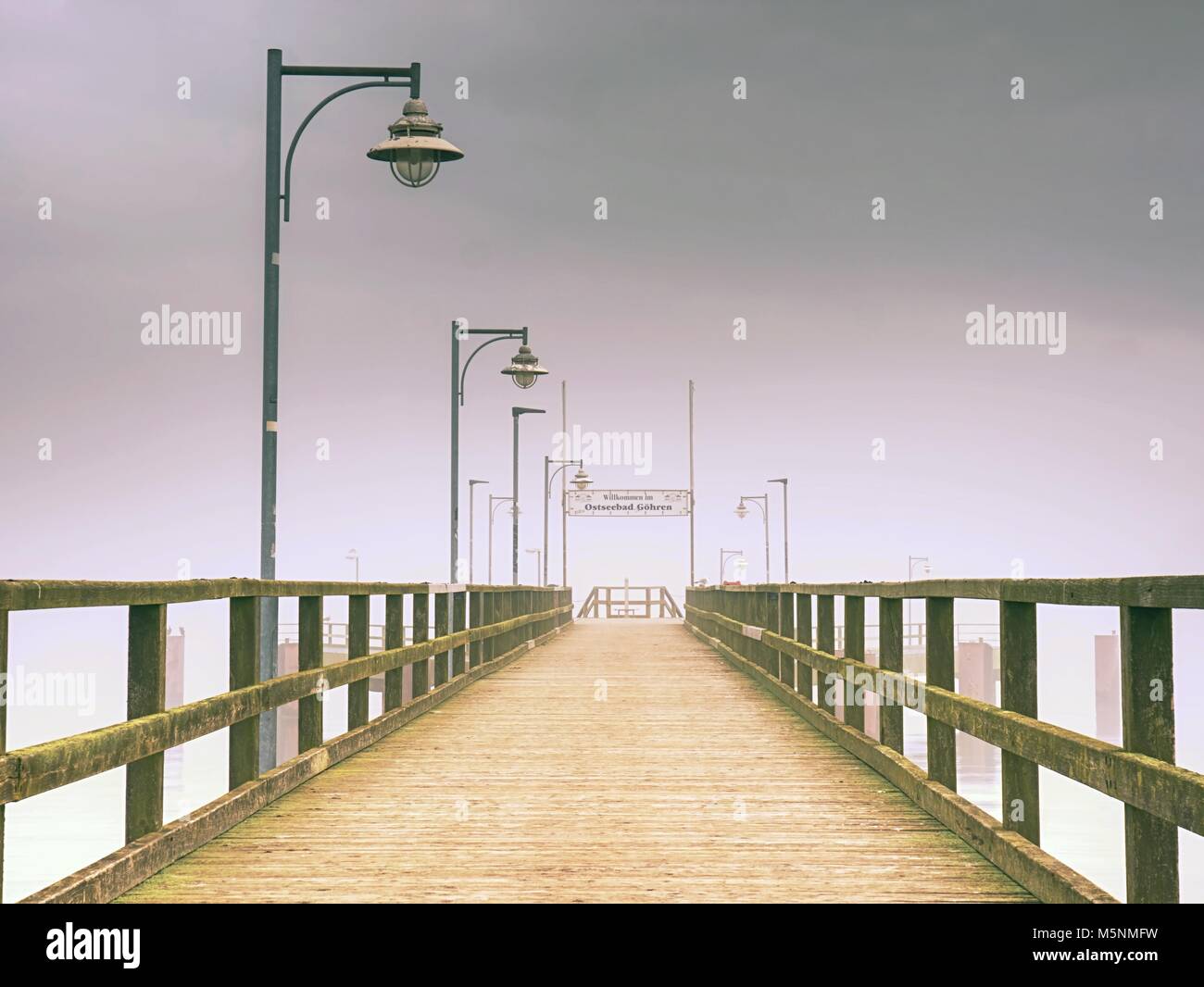 Empty wooden pier in harbor. Steel lamp post, horizon hidden in thick ...