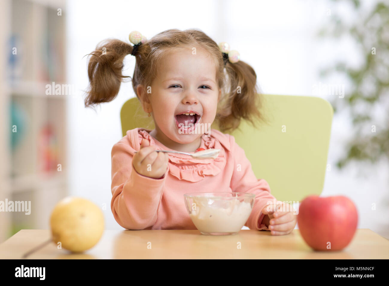 cheerful baby child eating food itself with a spoon Stock Photo - Alamy