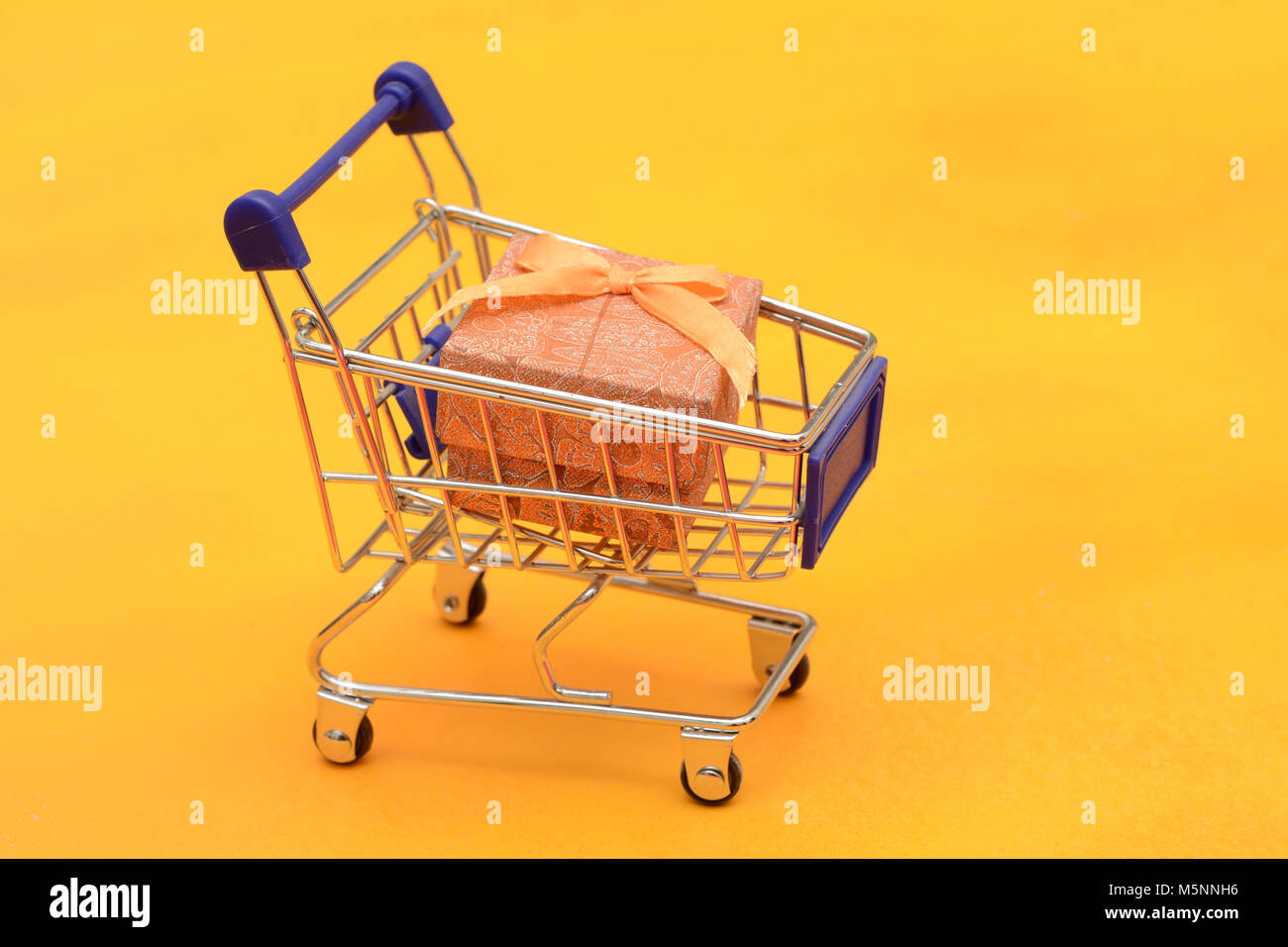 Gift box inside a shopping cart on yellow background Stock Photo - Alamy