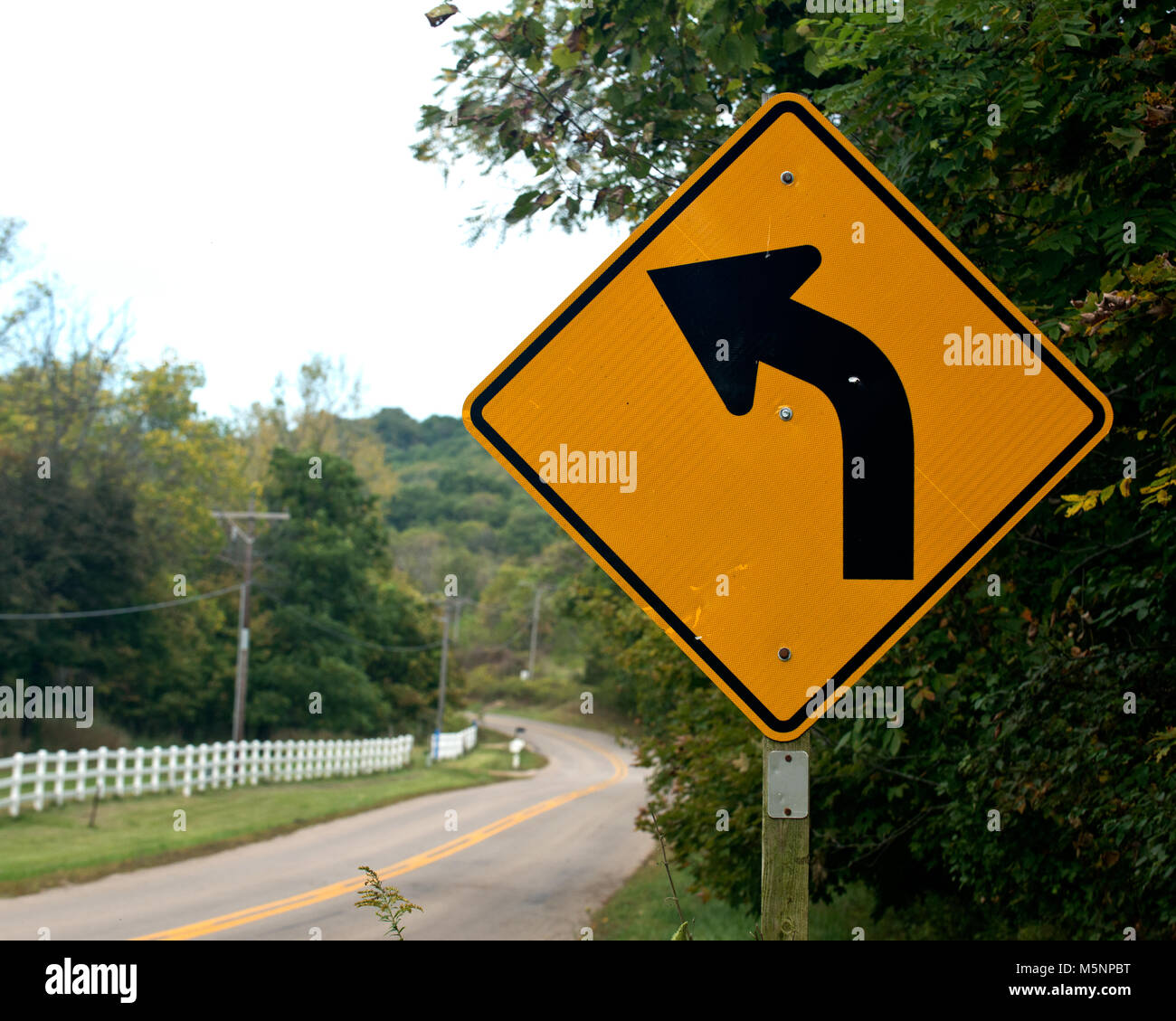 Yellow road sign indicating left turn on country road Stock Photo - Alamy