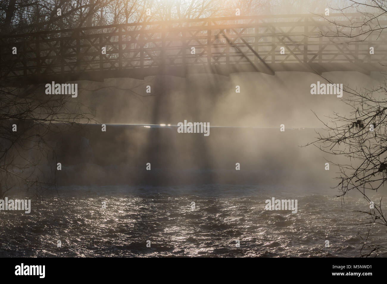 bridge extending over a dam with sun rays shining through Stock Photo ...