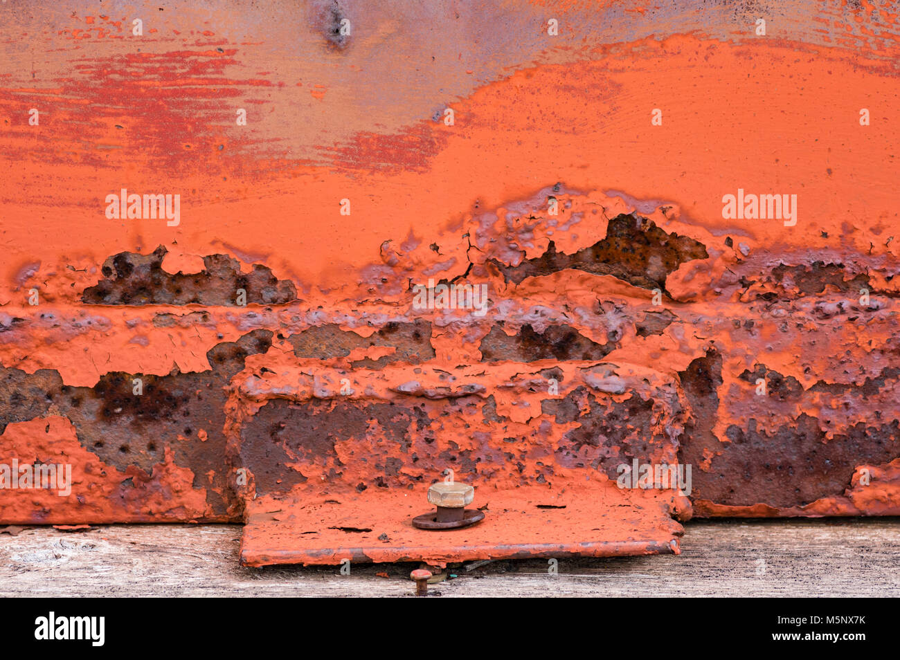 Orange painted metal with peeling paint and rust bolted to a wooden ...