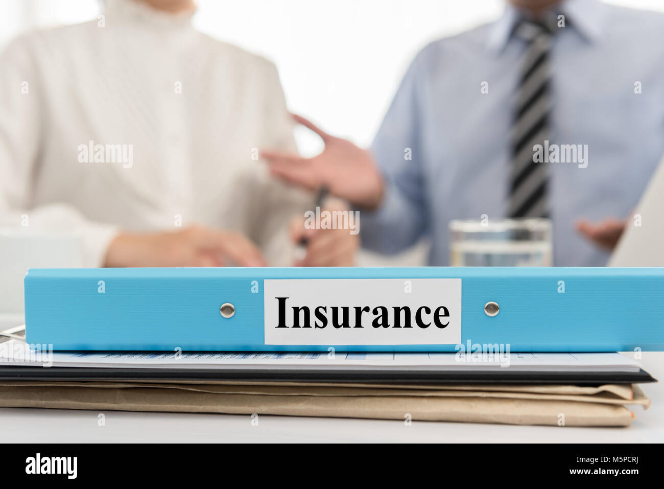 closeup insurance file with two business people meeting in office ...