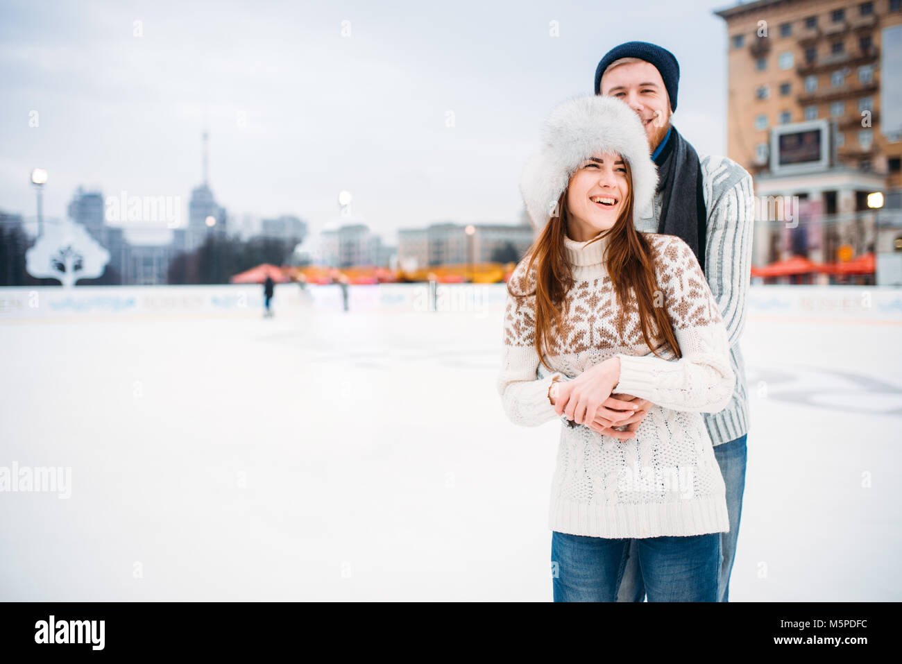 Happy love couple hugs on skating rink. Winter ice-skating on open air ...
