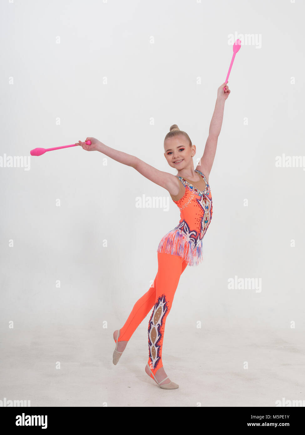 A young gymnast in an orange sports suit stands on a white background ...
