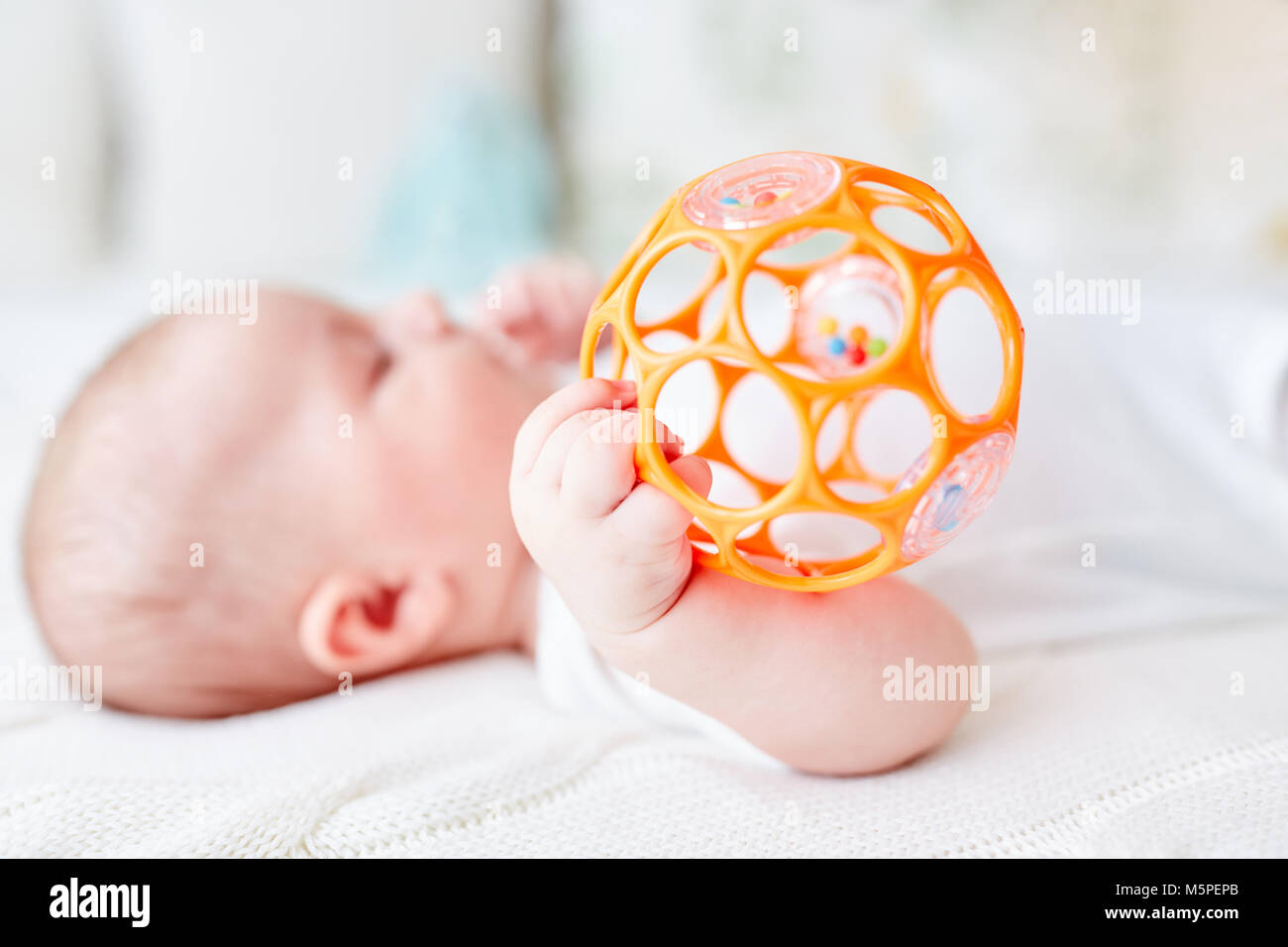 Little baby is lying on his back holding the rattle with one hand Stock ...