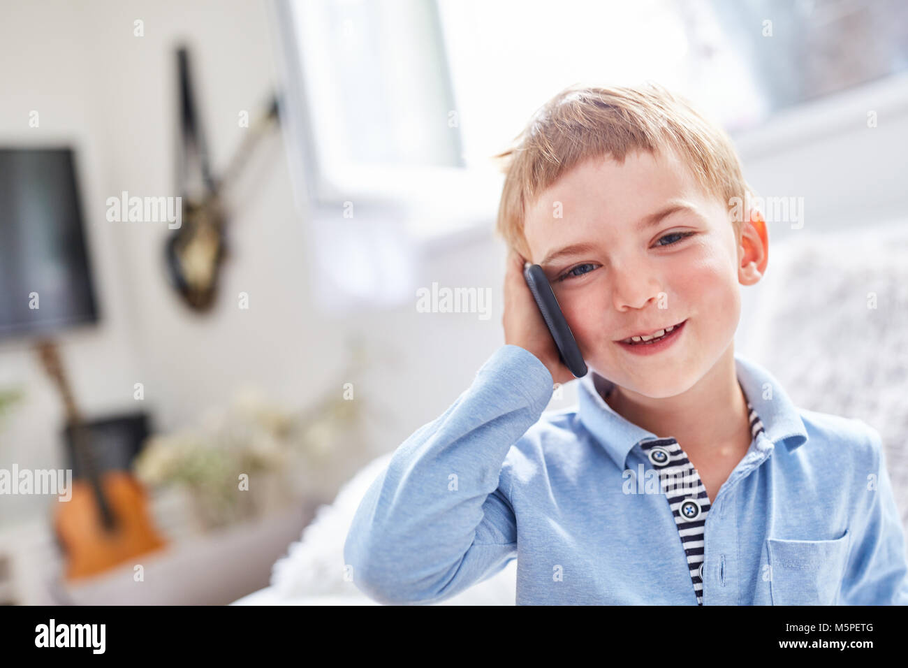 Happy boy is phoning with mobile phone or smartphone in the apartment ...