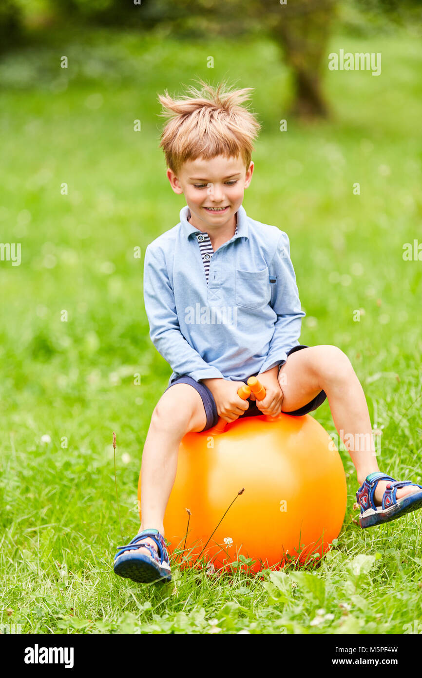 Smiling boy is having fun in the park and jumping on a hopping ball ...