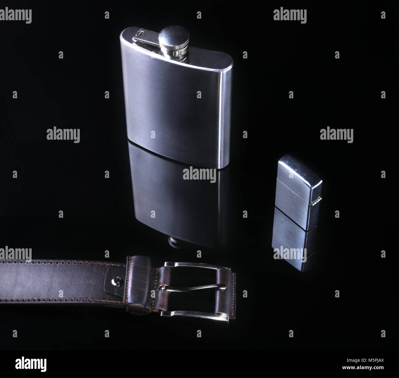 Stainless hip flask, lighter and luxury belt isolated on mirror black ...