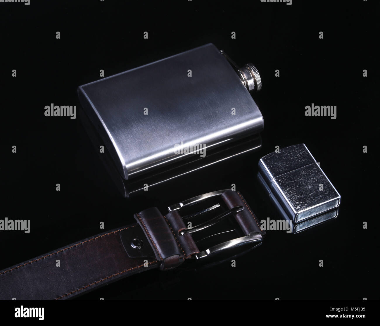 Stainless hip flask, lighter and luxury belt isolated on mirror black ...
