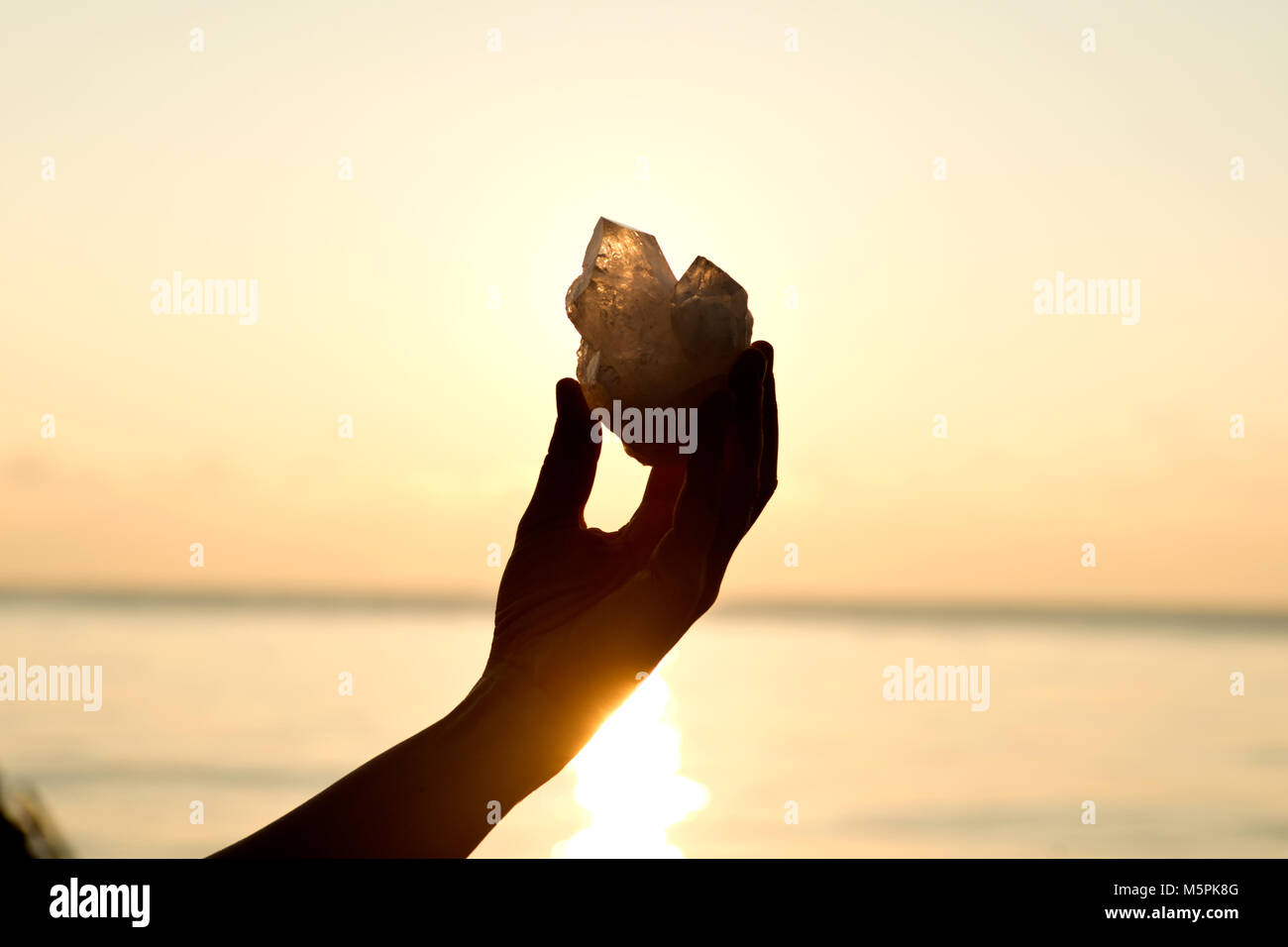Young woman's hands holding clear quartz point in front of the lake ...
