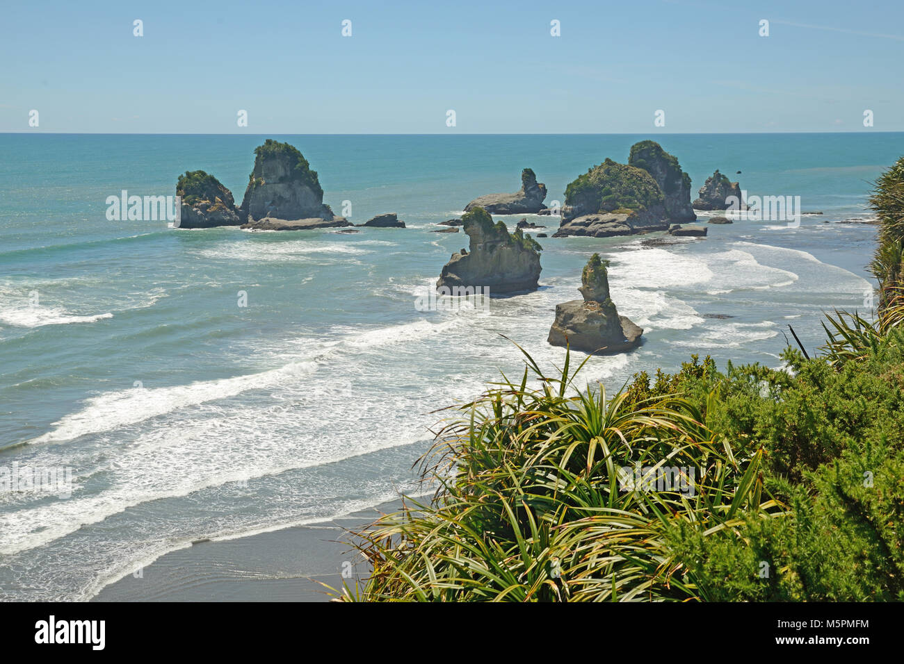 native bush frames a beach at low tide on a West Coast beach, South ...