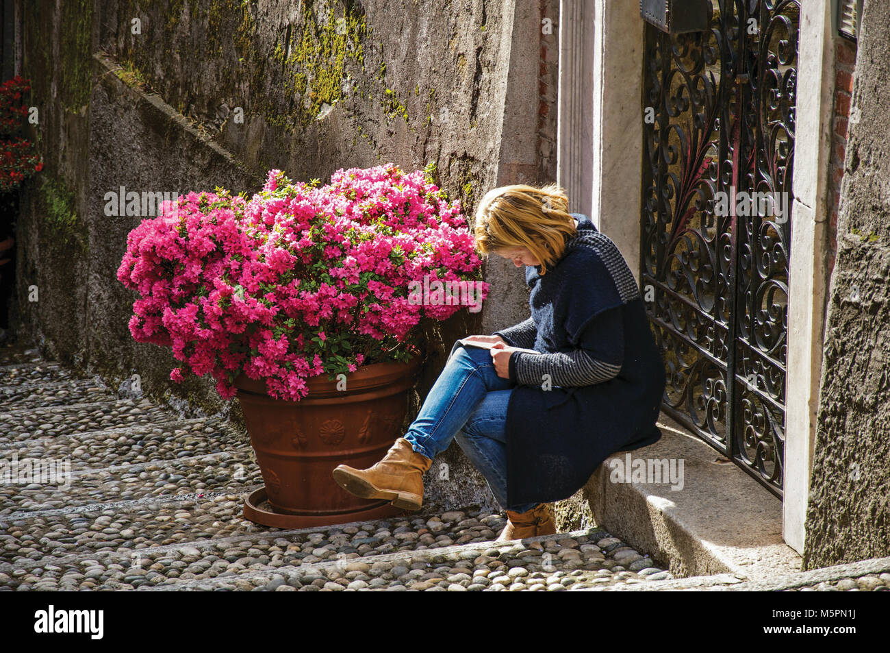 Como, Italy. View of alley in hillside and woman reading in front of a ...