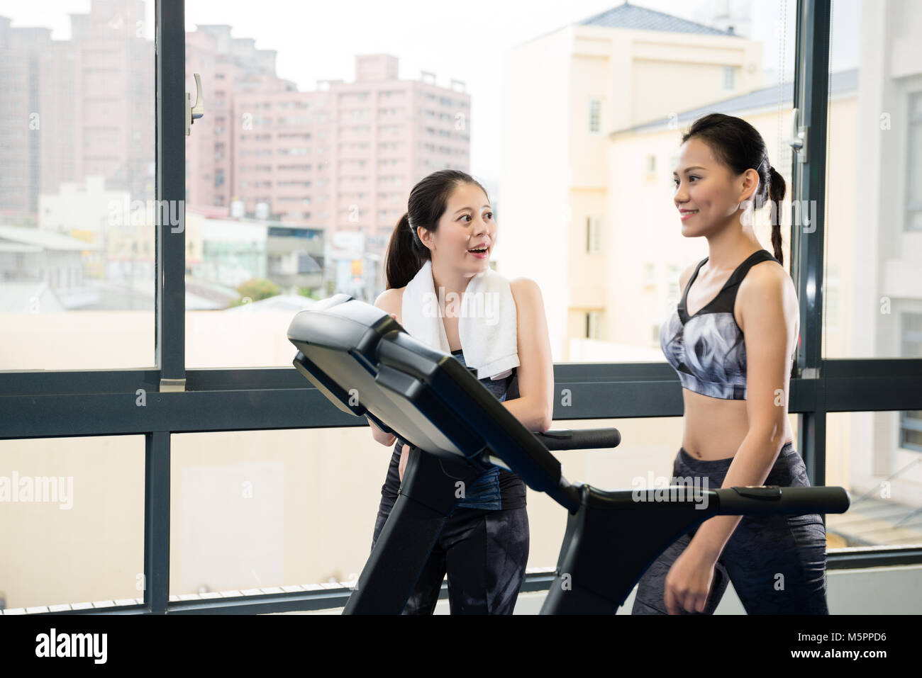 girl meet and talking to her friend who walking on treadmill machine ...