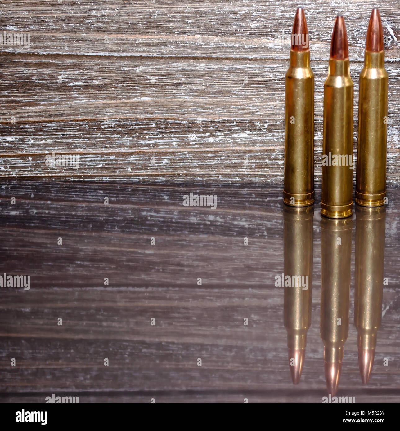 Three rifle bullets with a wooden background and on a reflective ...