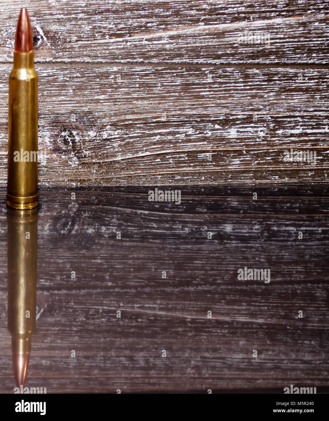 A single rifle bullet with a wooden background and on a reflective ...