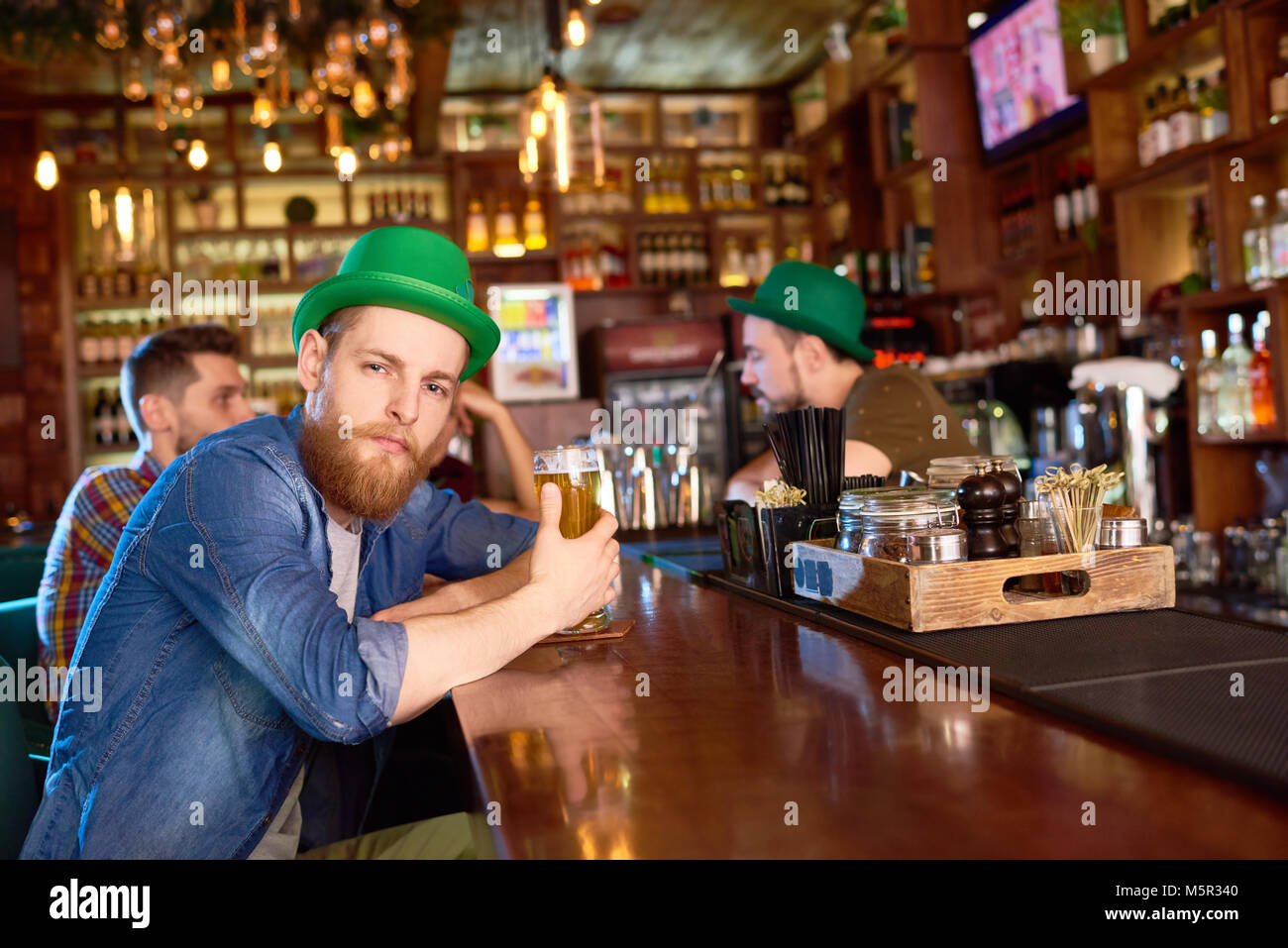 Confident young man with bushy beard wearing denim shirt and green ...