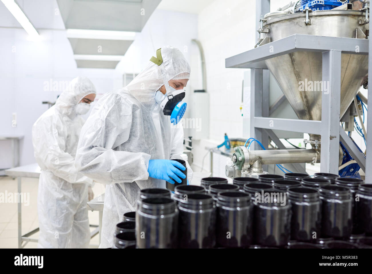 Group of concentrated factory workers wearing coveralls, respirators ...