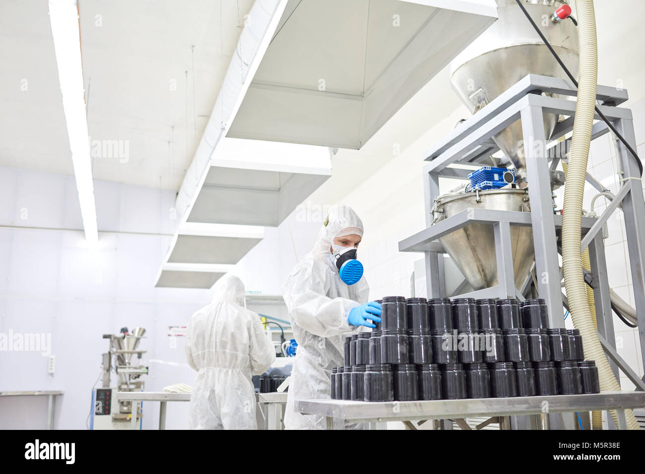 Two pharmaceutical factory workers wearing coveralls and respirators ...