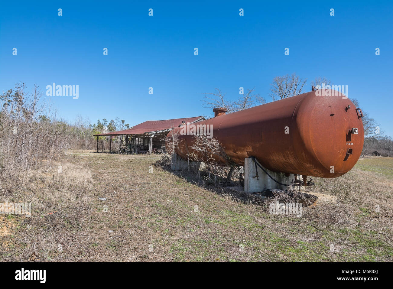A rusty, 1000 gallon LP gas tank with a rustic, weathered, old barn in ...