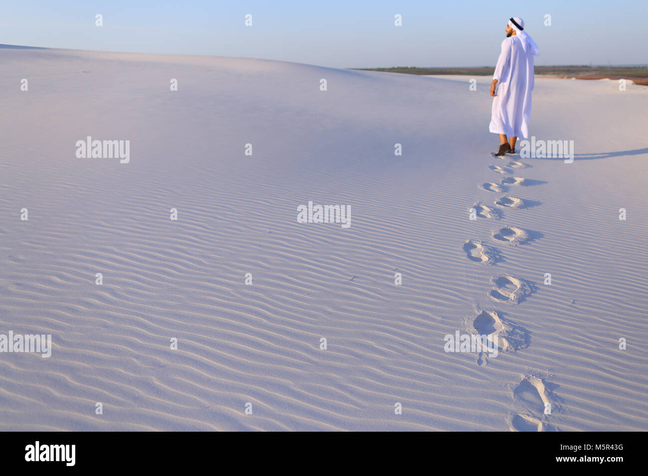 Joyful male Muslim walks through white sand desert and enjoys li Stock ...
