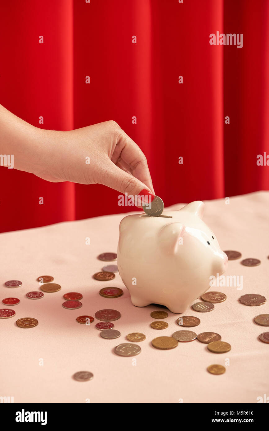 A female hand hold a coin and insert into pig coin bank Stock Photo - Alamy