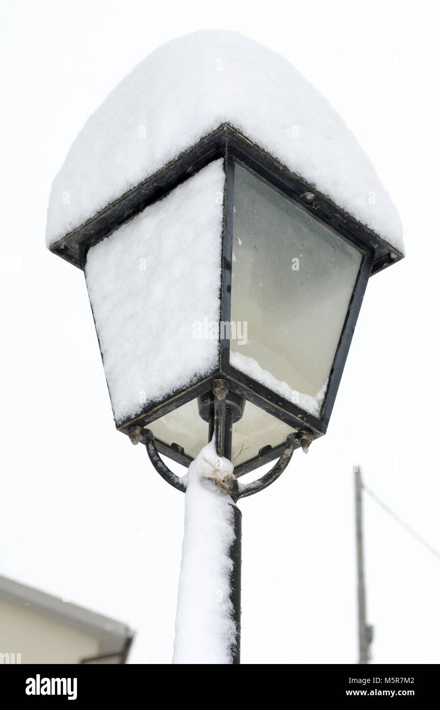 Pile of snow on street lamp, with white sky during a snowfall, vertical ...