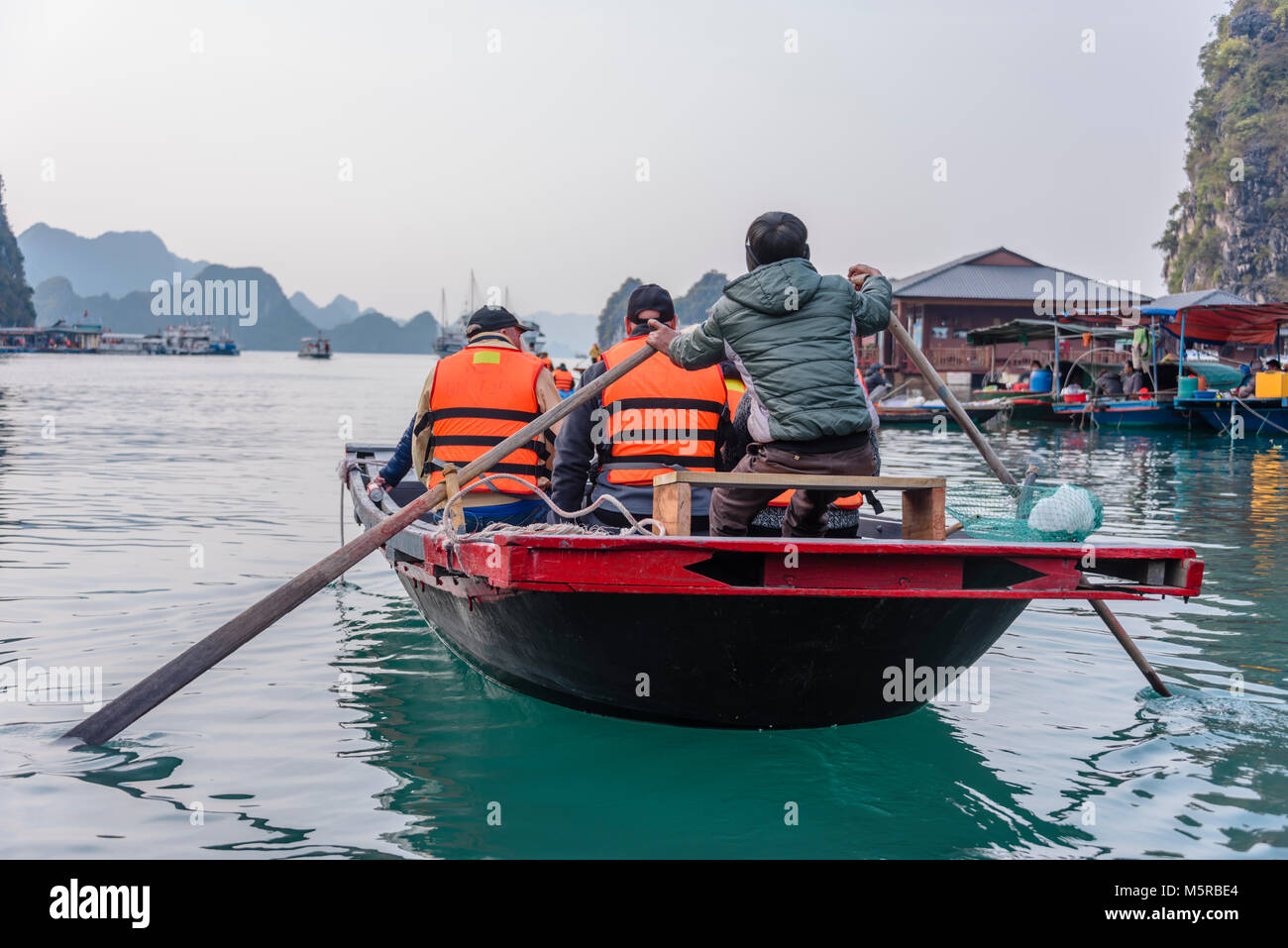Tourists wearing orange life jackets are taken in rowing boats around ...
