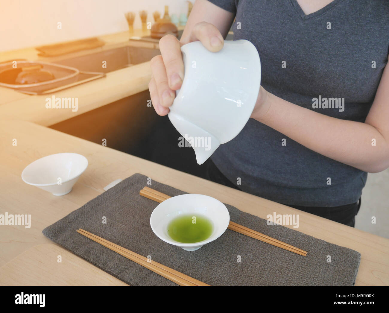 Female pouring green tea to white small ceramic cup on grey clothe mat ...