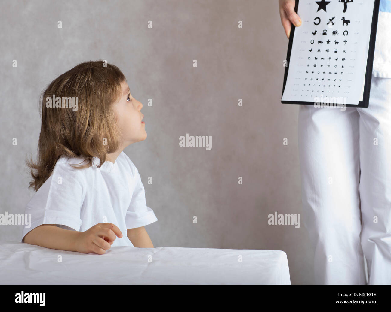 Ophthalmologist checks vision of 5 years old boy by means of eye chart ...