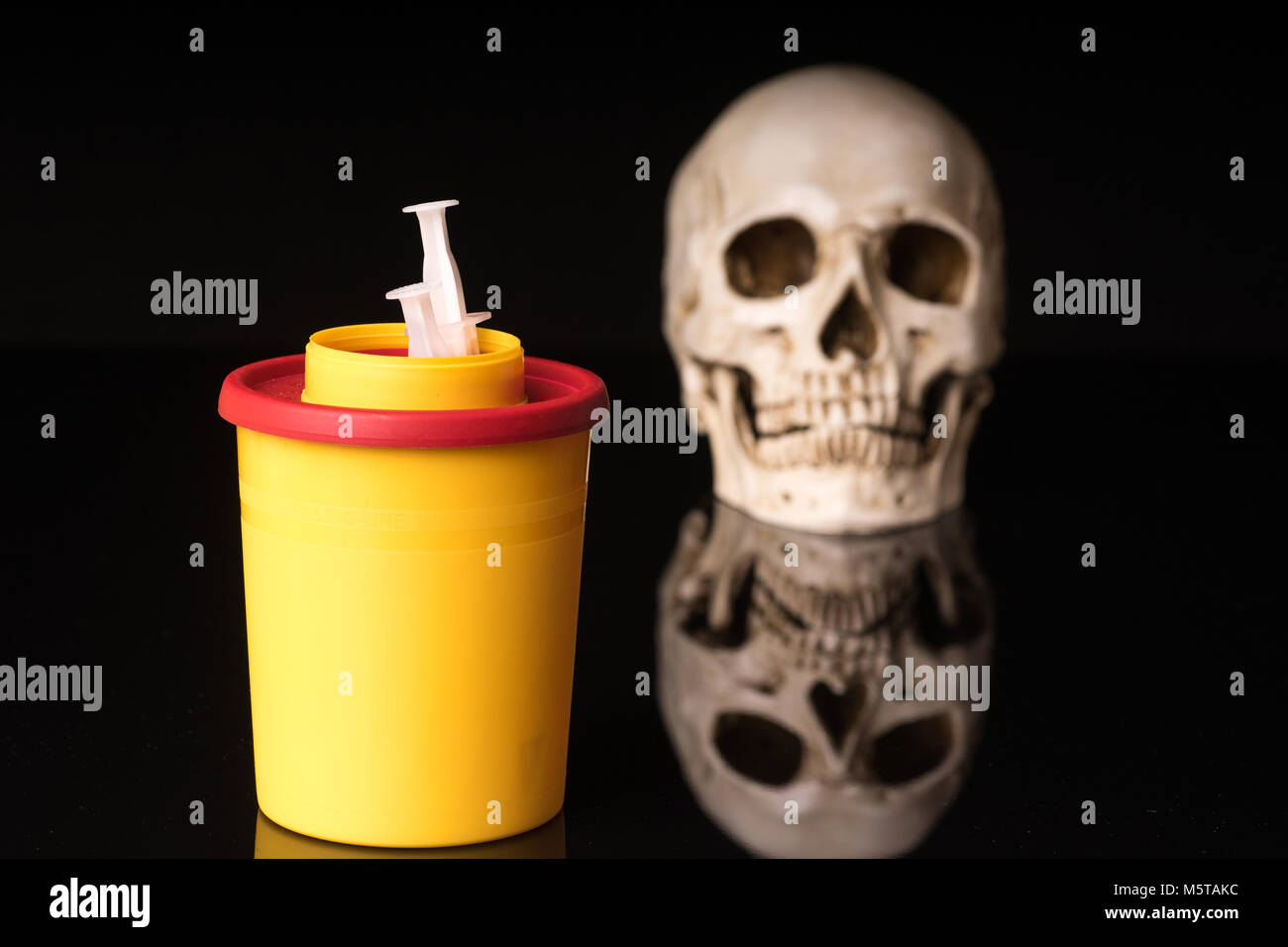 Skull, syringe and yellow waste container, isolated on black with ...