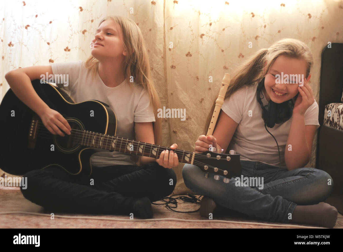 Two female teens playing musical instruments, guitar and flute, at home ...