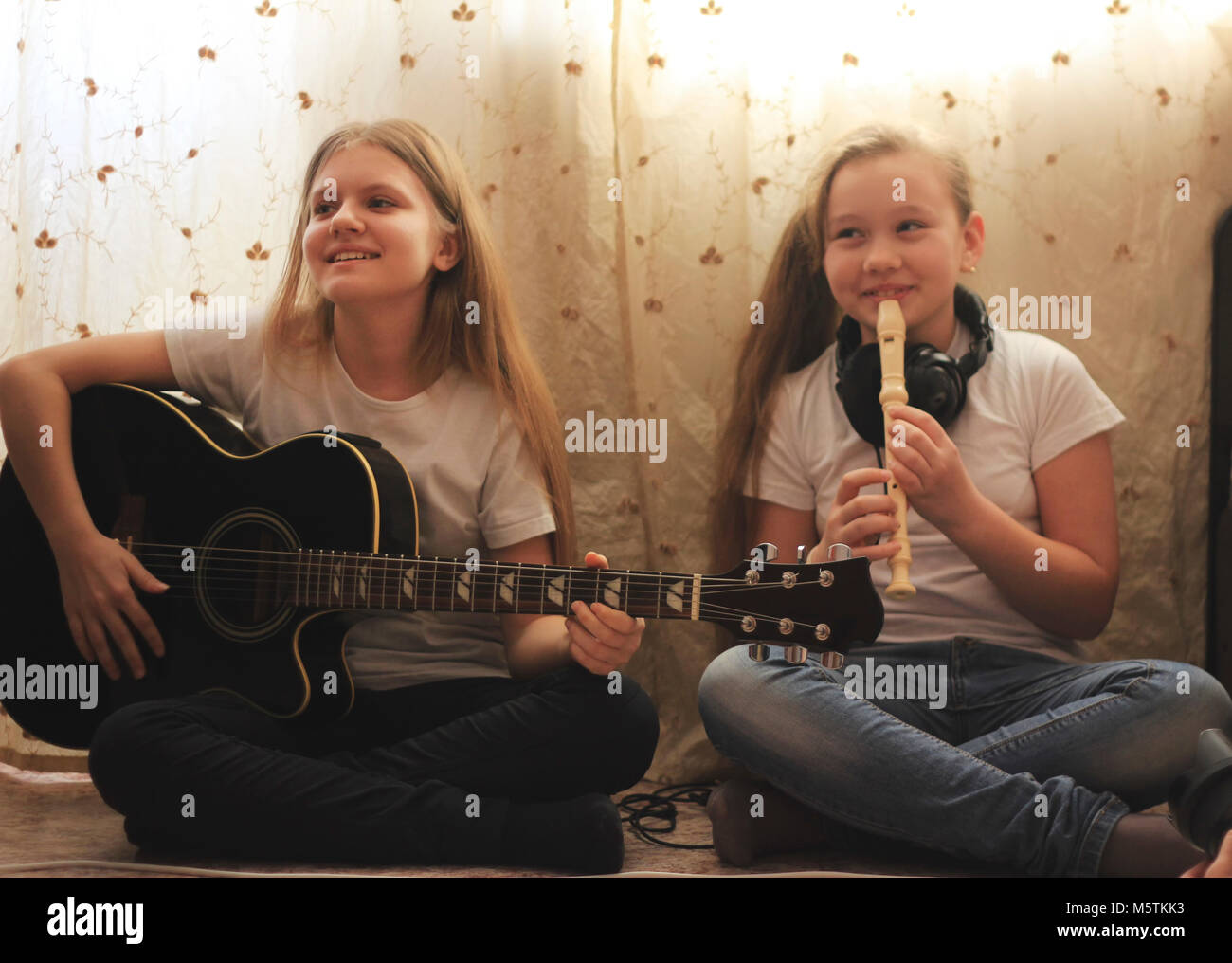 Two female teens playing musical instruments, guitar and flute, sitting ...