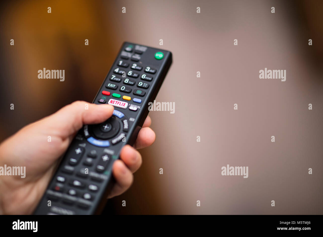 A person using a television remote with a dedicated Netflix logo on the ...
