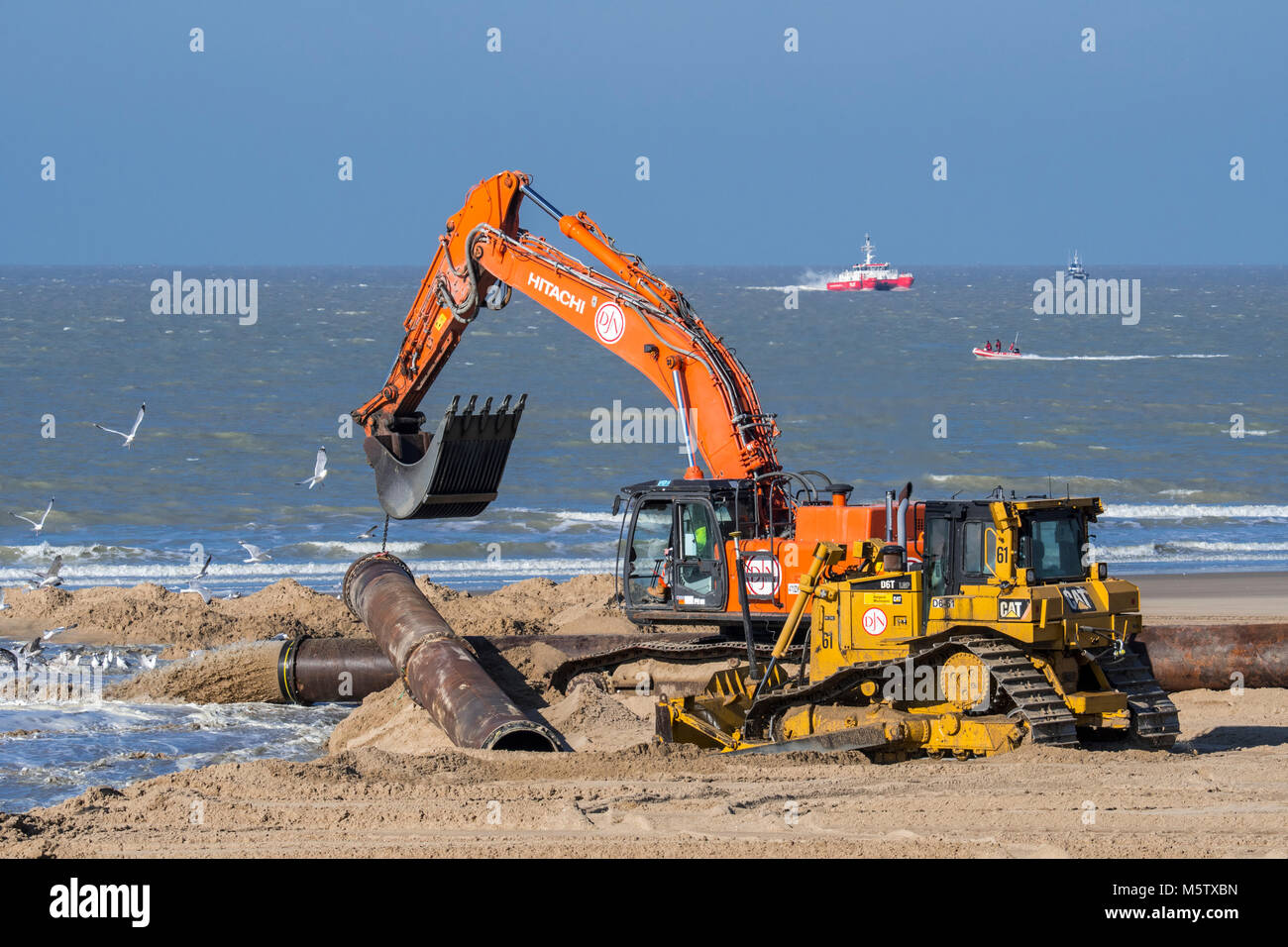 Bulldozer and hydraulic excavator installing pipeline during sand ...